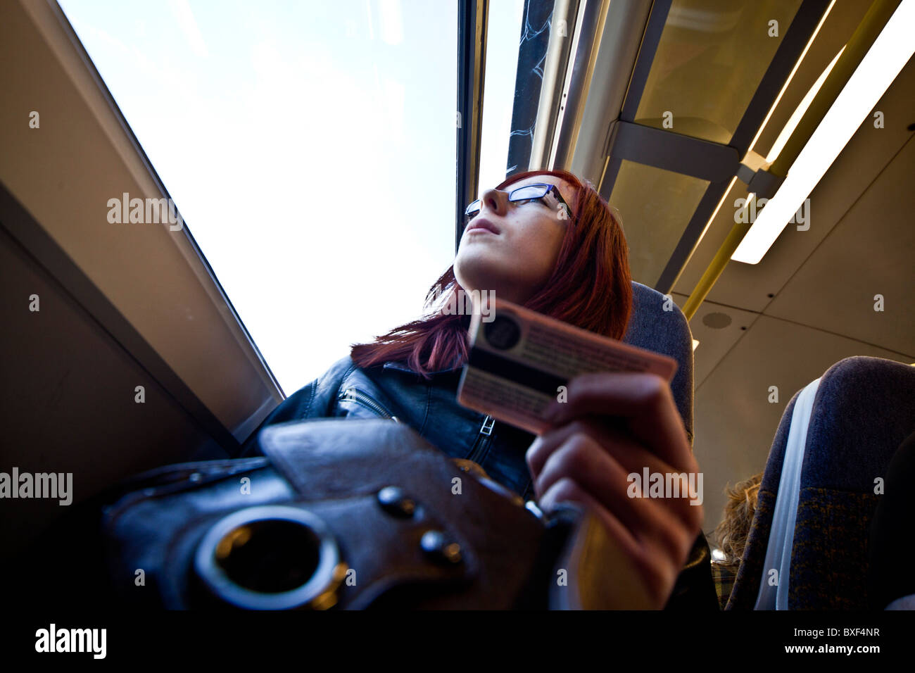Young woman sat on a train holding a ticket, looking out of the window ...