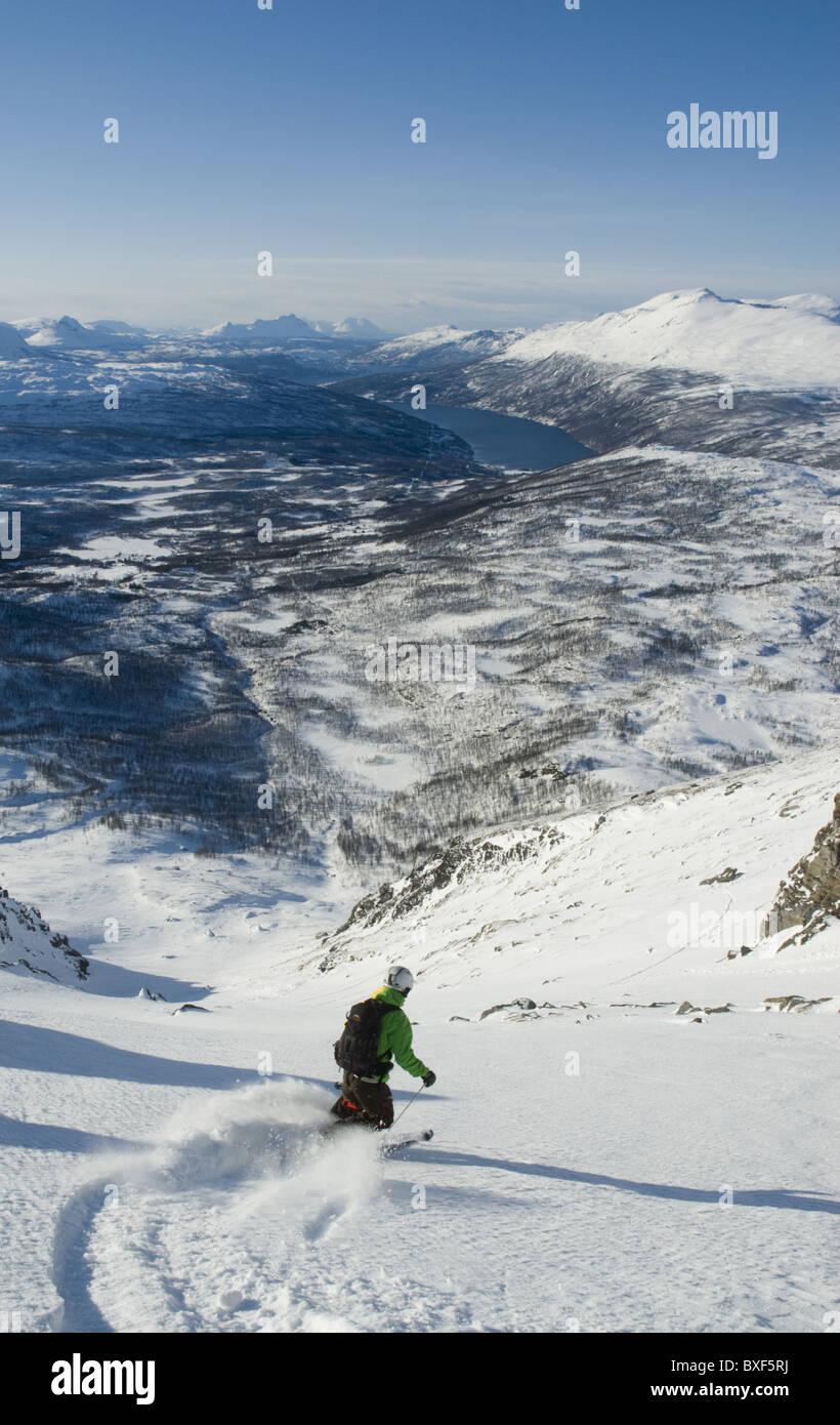 A male telemark skier making a telemark turn in powdery snow in a steep ...