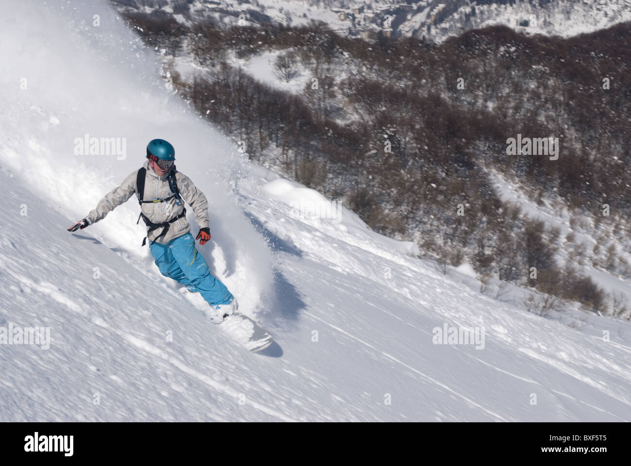 A snowboarder making a turn in deep powder snow, with a snowy forest in ...