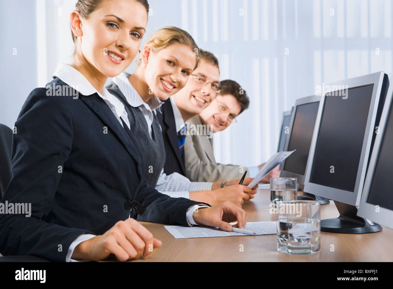 Portrait of confident people sitting in a line in front of monitors and ...