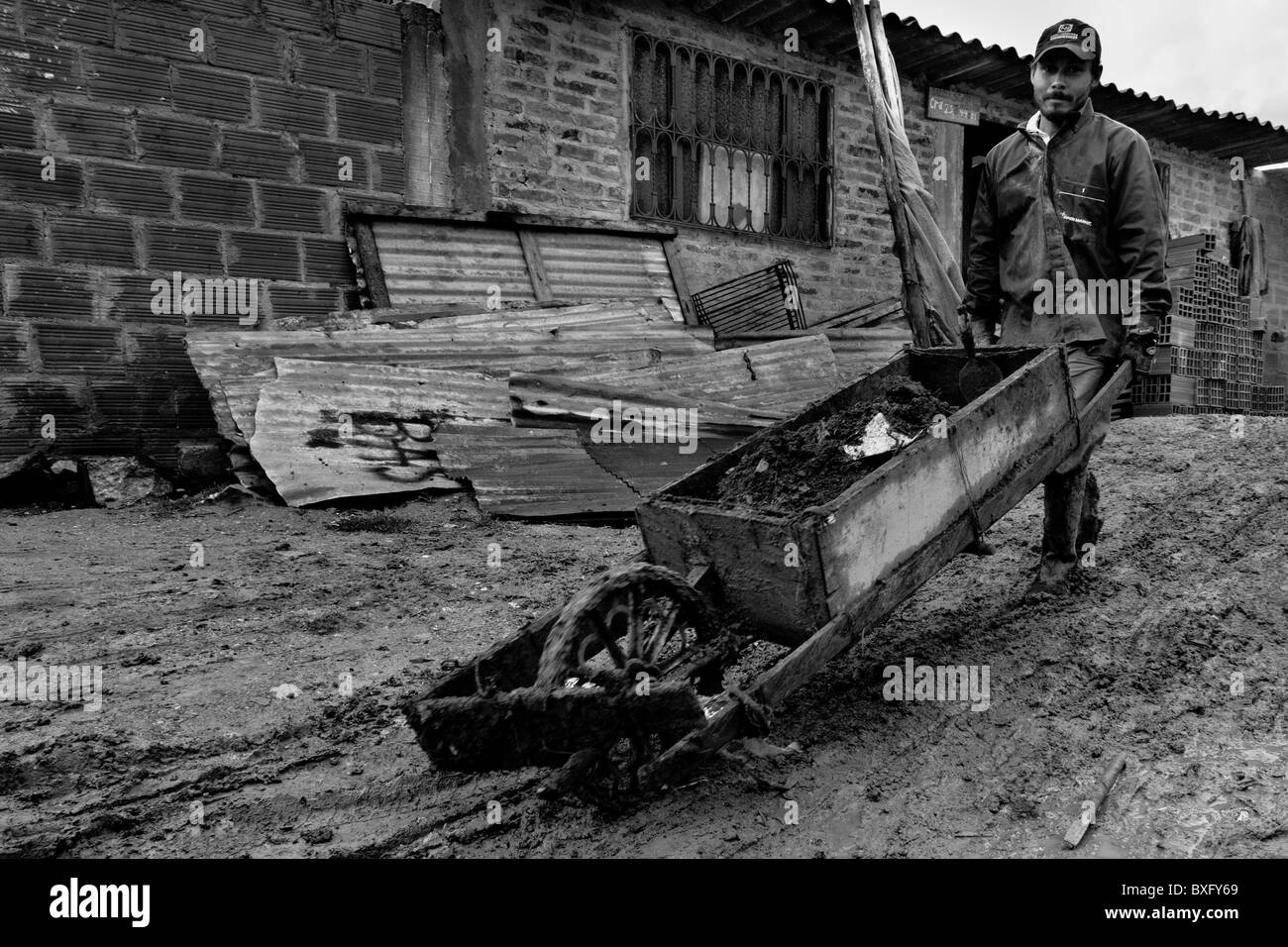 A displaced man pushs a wheel barrow in the mud while building a new ...