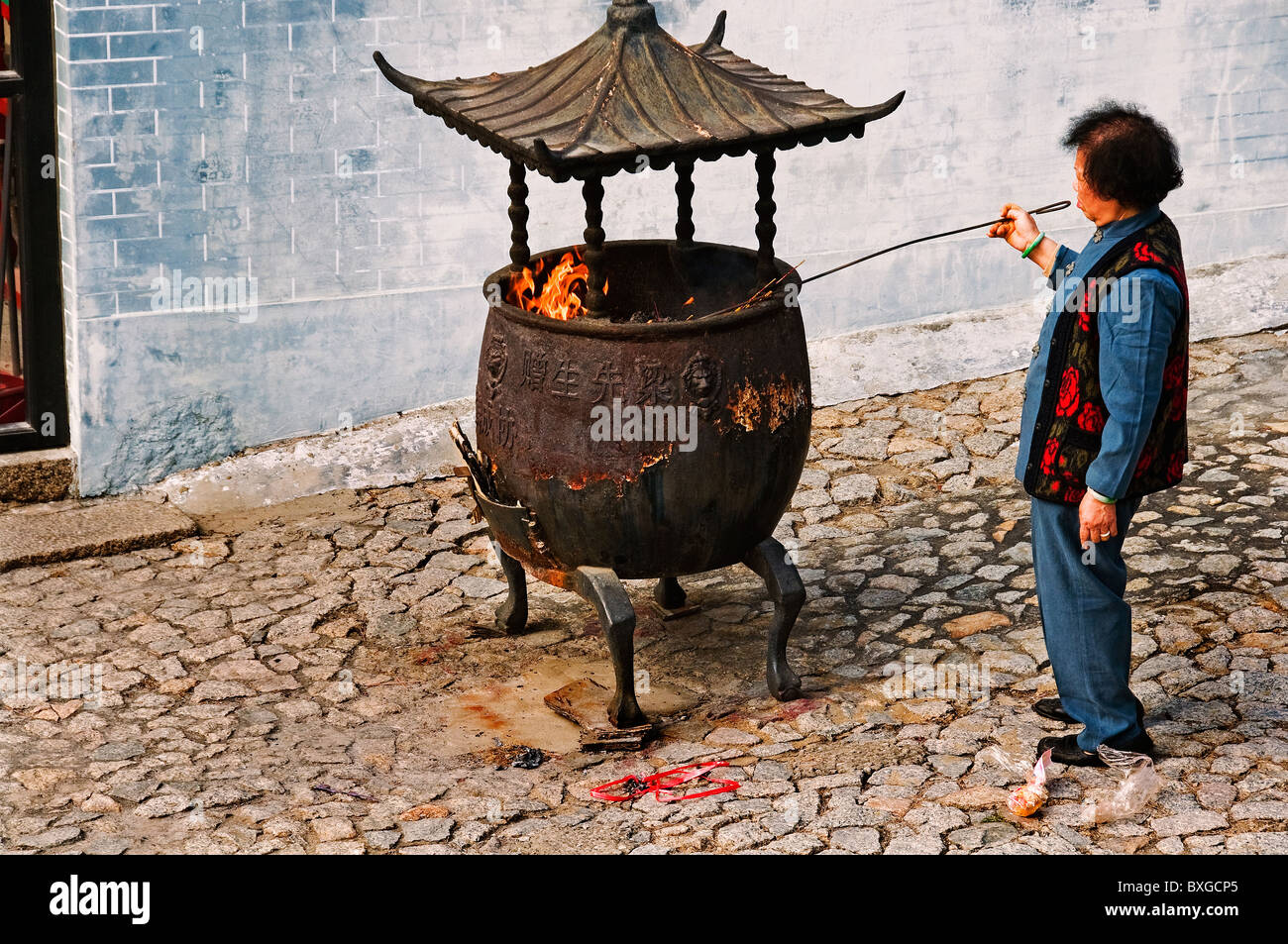 Oriental woman tending burning fire in shrine outside of Buddhist ...