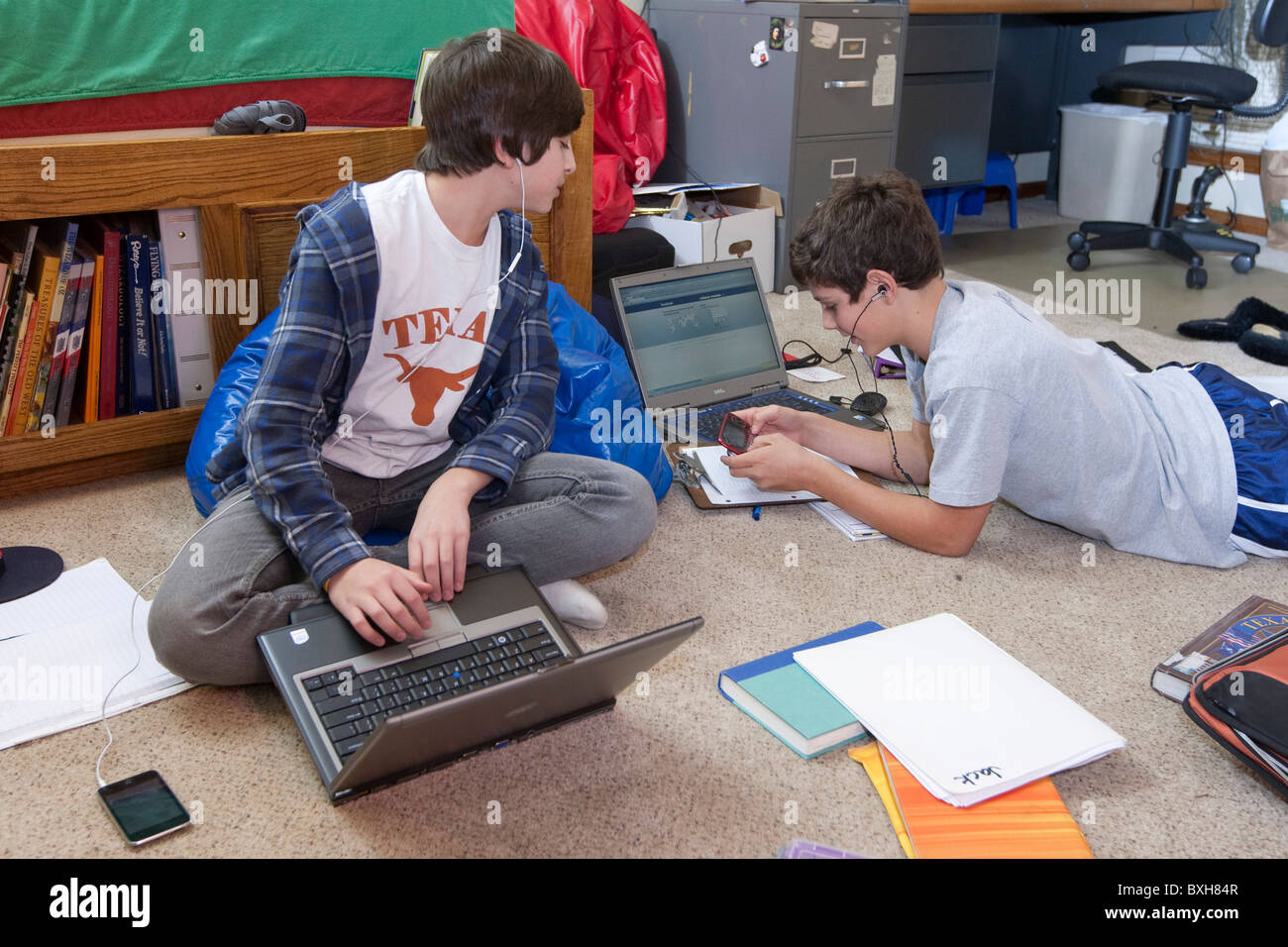 Teen boys in bedroom with laptop computer and textbooks, listening to ...