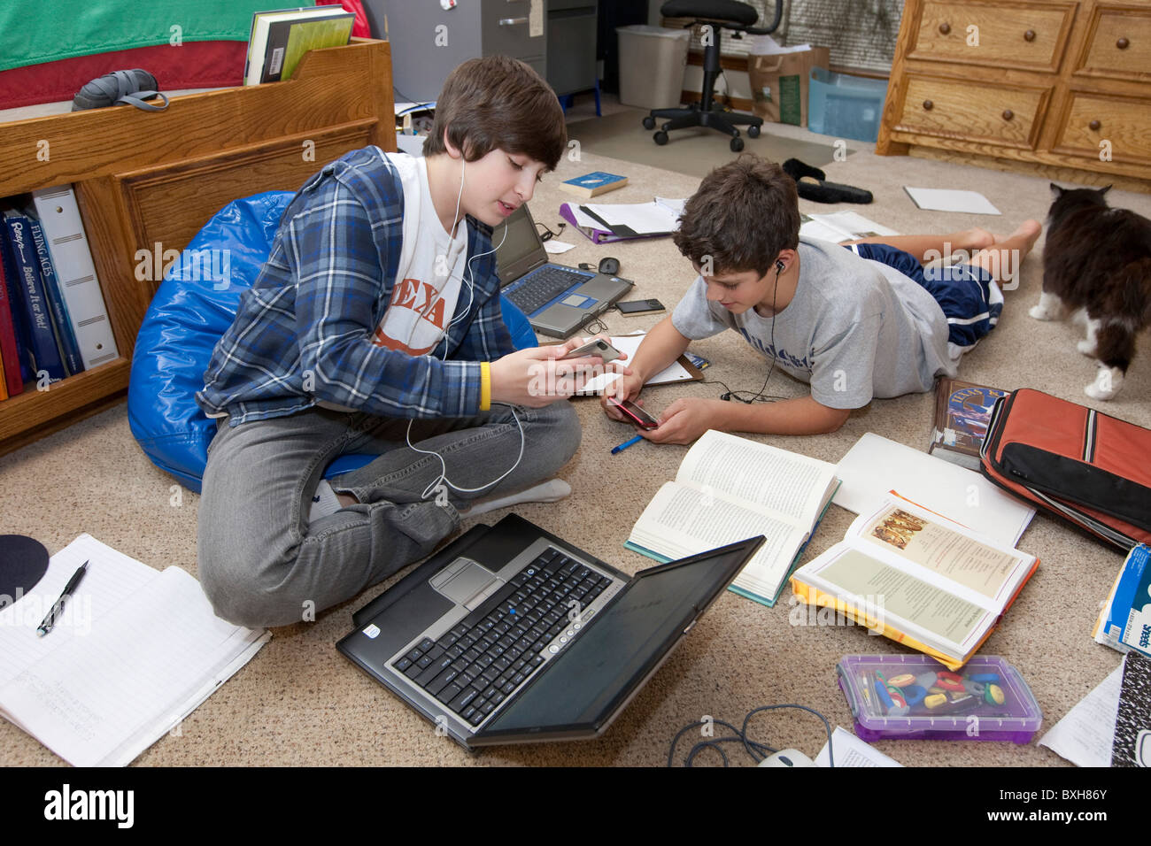 Teen boys in bedroom with laptop computer and textbooks, listening to ...