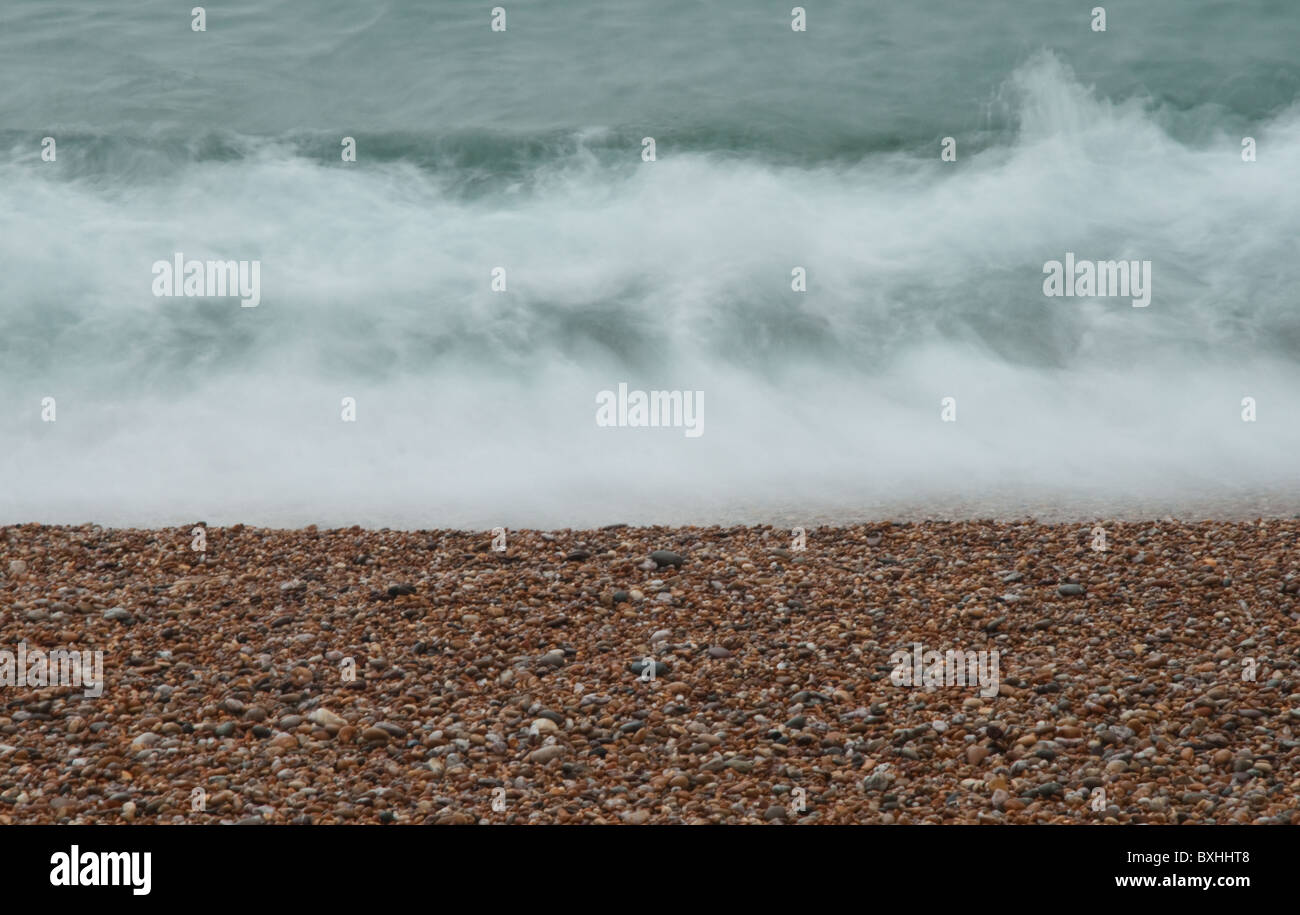 A wave crashing onto the shingle beach taken with a slow shutter speed ...