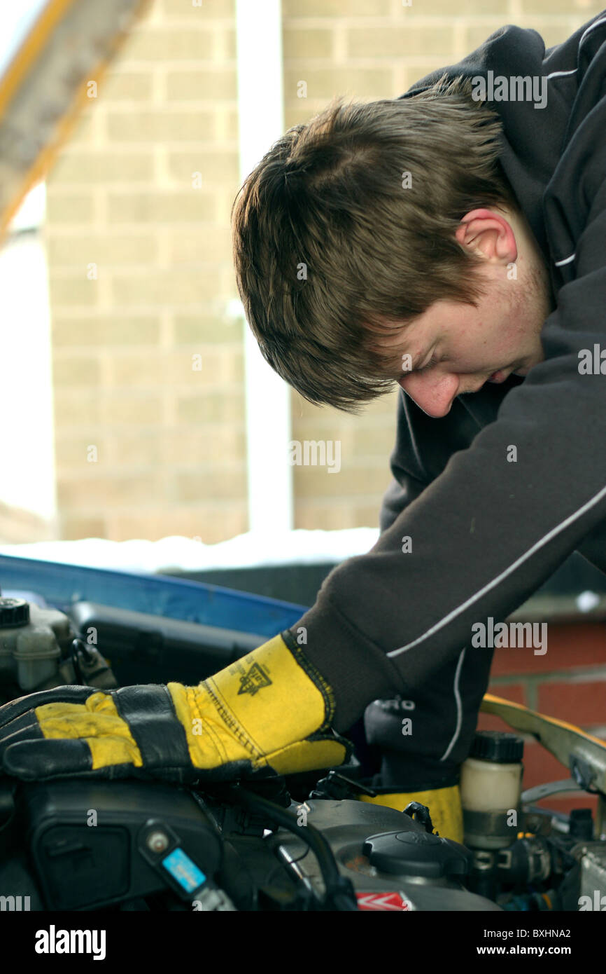 A young Caucasian male mechanic working under the bonnet of a car ...