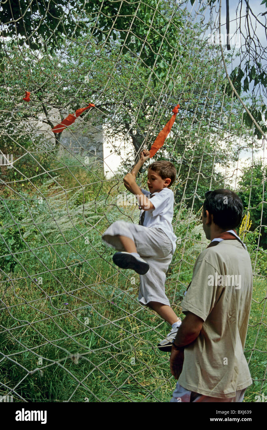 Boy scout climbing a large net under supervision of a scout leader ...