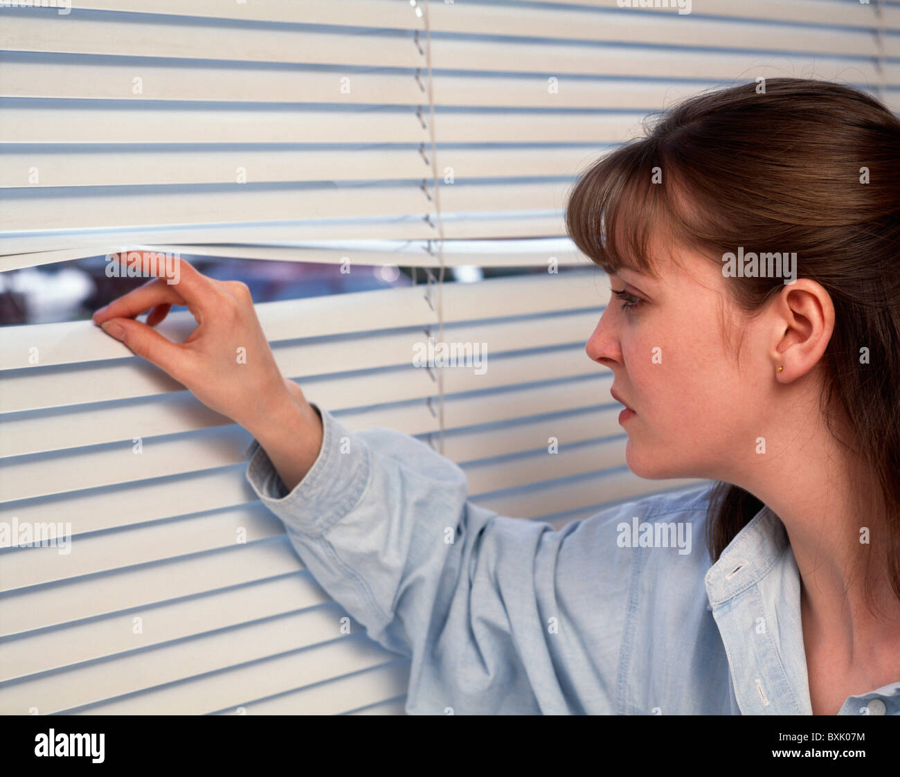 Frightened English girl looking through window blinds Stock Photo - Alamy