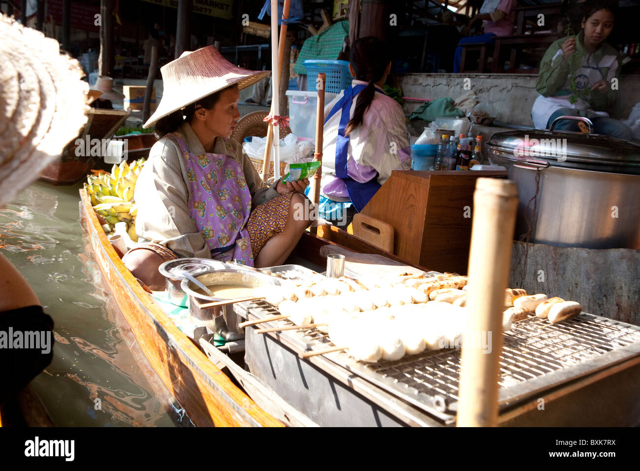 Vendor in traditional straw hat riding through the Damnoen Saduak ...