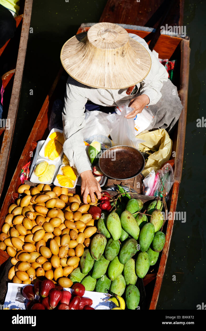Vendor in traditional straw hat riding through the Damnoen Saduak ...