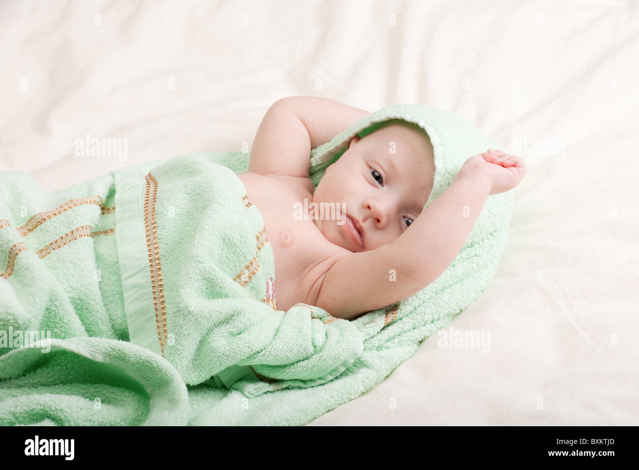 Ten weeks old cute little baby girl wrapped in towel stretching in bed ...