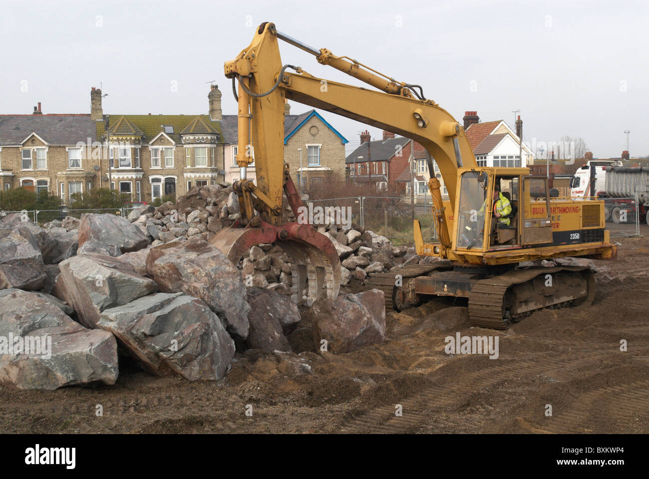 Tracked grab lift picking up boulder for use in sea defence Felixstowe ...