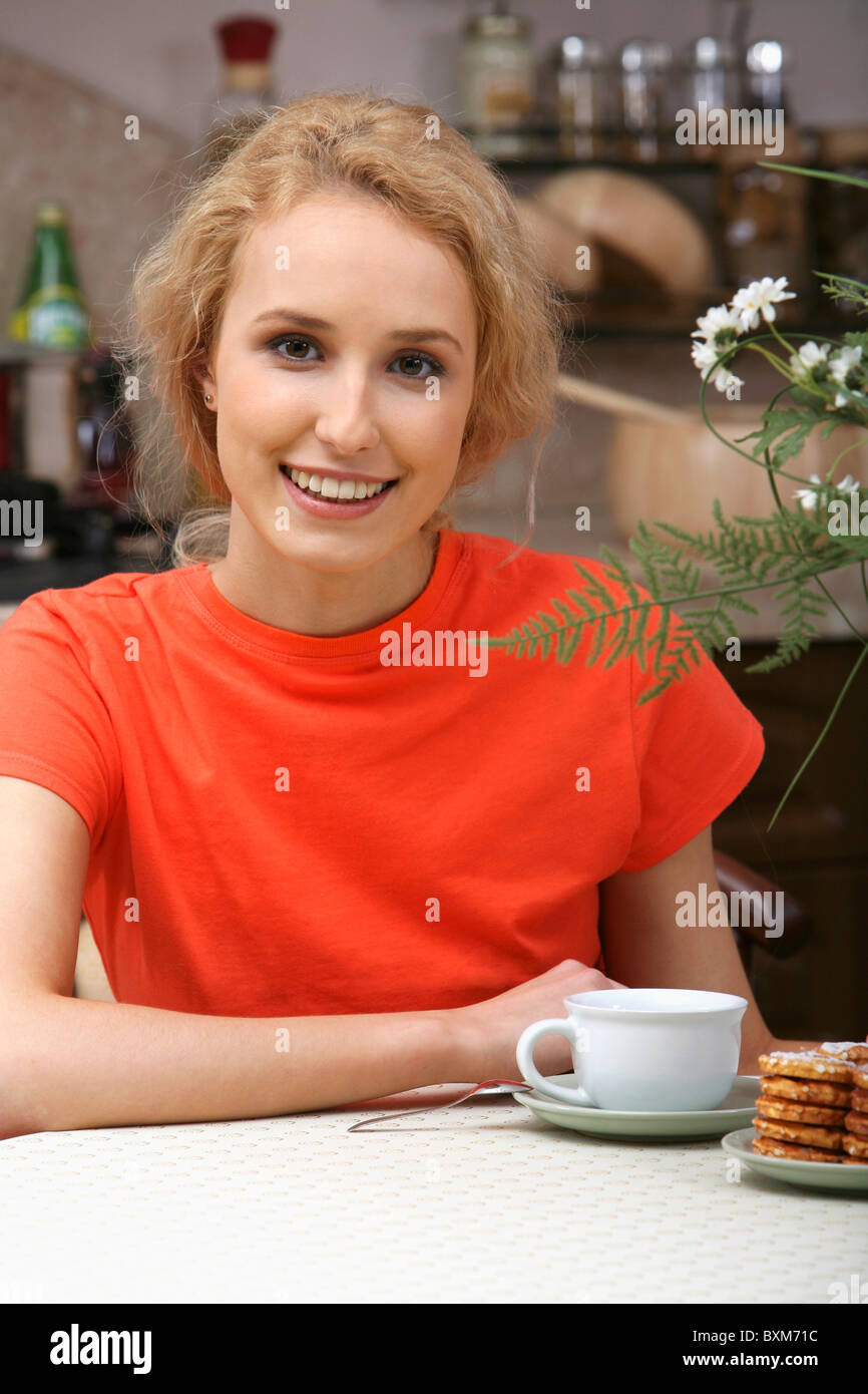 Portrait of smiling beautiful woman sitting at the table in the kitchen ...