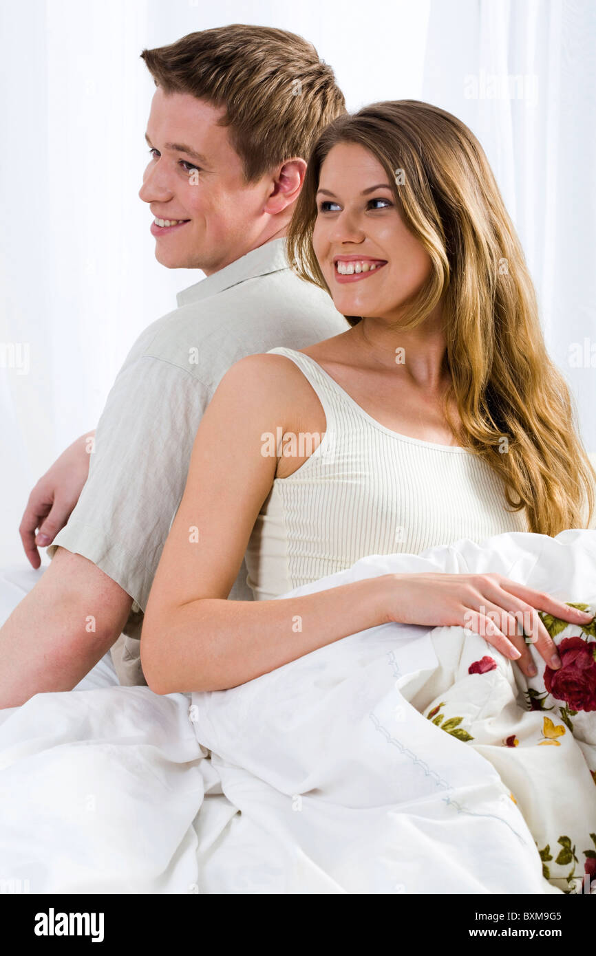 Young laughing couple sitting back to back on the bad Stock Photo - Alamy