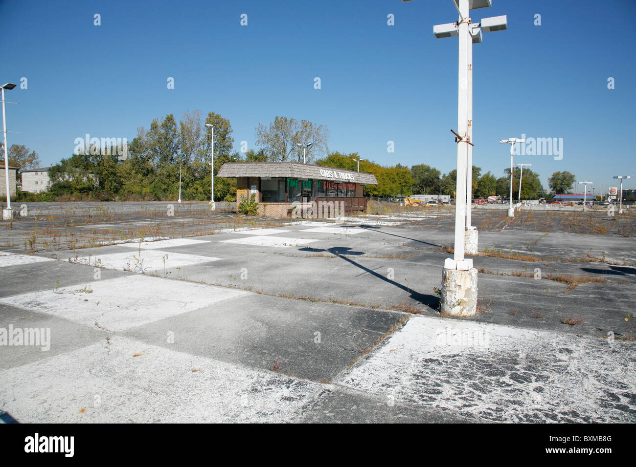 Empty abandoned car and truck dealer lot with weeds growing. Sign reads ...