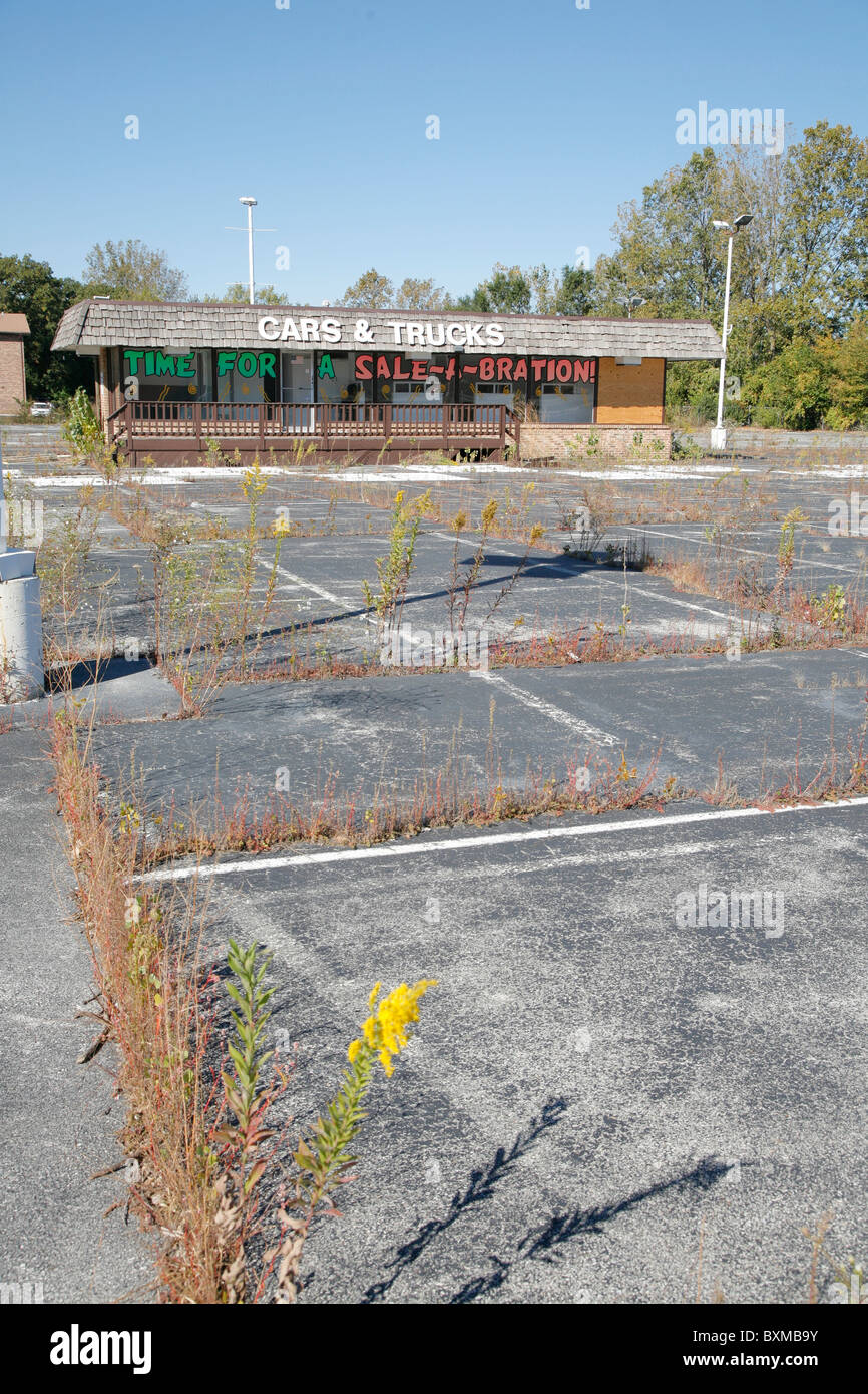 Empty abandoned car and truck dealer lot with weeds growing. Sign reads ...