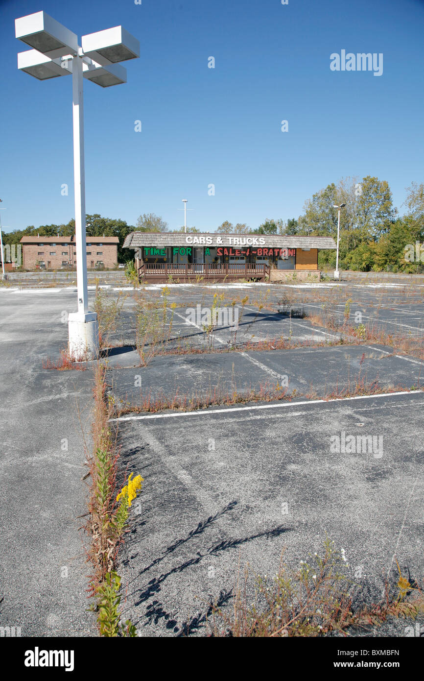Empty abandoned car and truck dealer lot with weeds growing. Sign reads ...