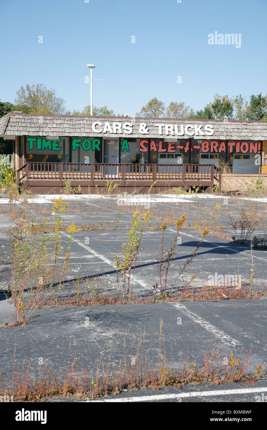 Empty abandoned car and truck dealer lot with weeds growing. Sign reads ...