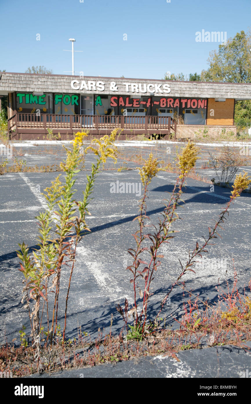 Empty abandoned car and truck dealer lot with weeds growing. Sign reads ...