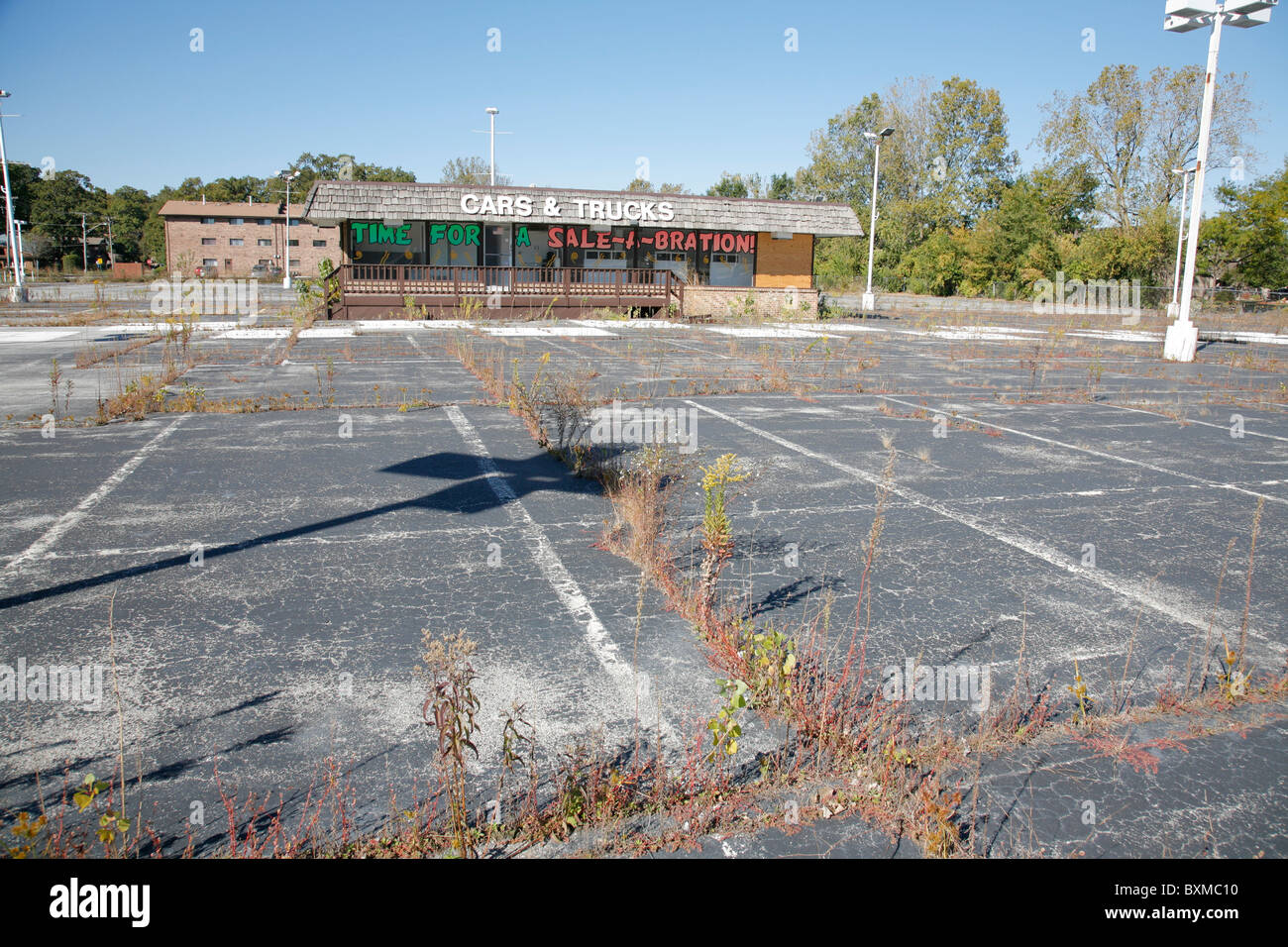 Empty abandoned car and truck dealer lot with weeds growing. Sign reads ...