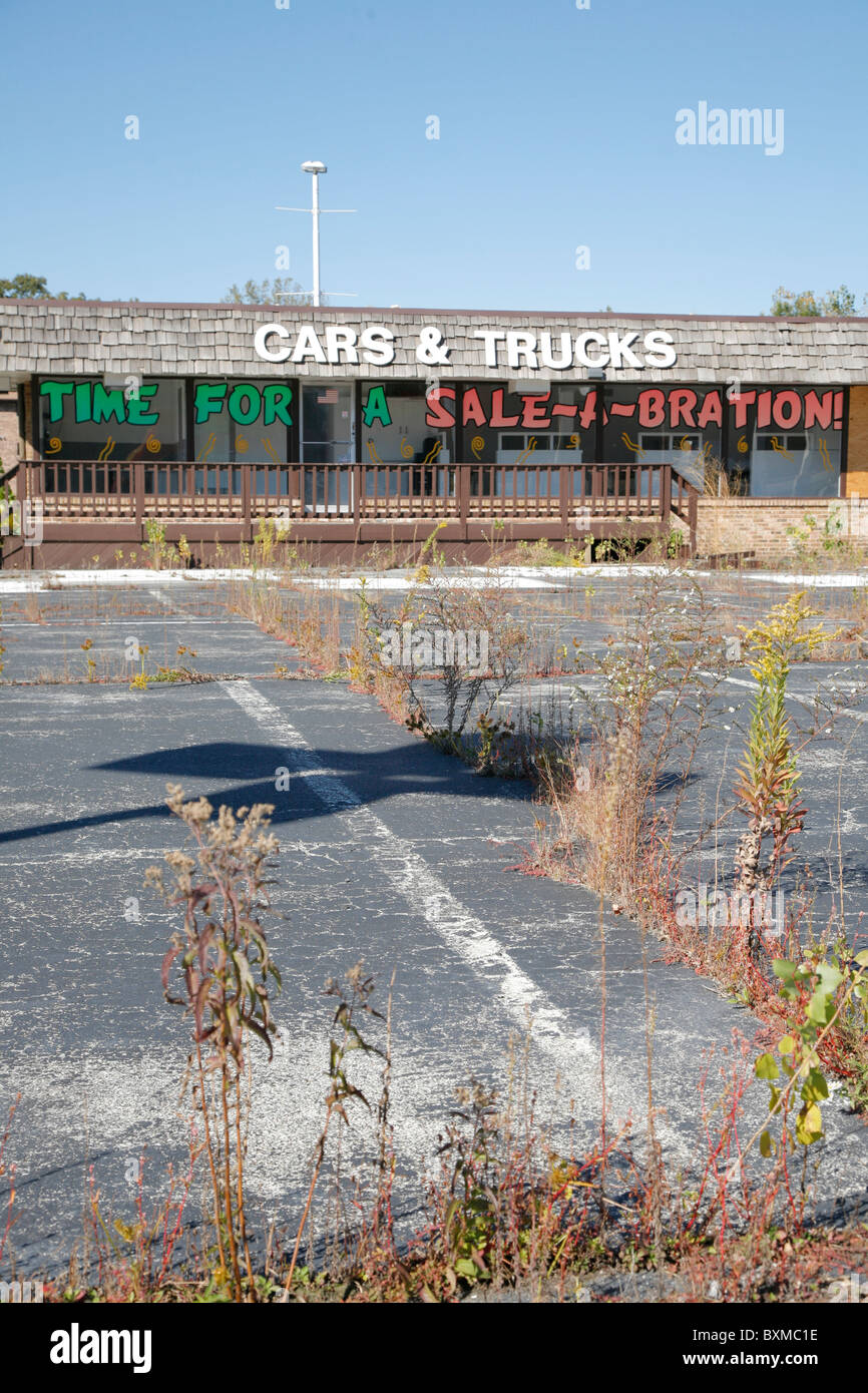 Empty abandoned car and truck dealer lot with weeds growing. Sign reads ...