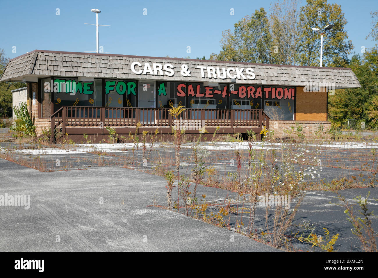 Empty abandoned car and truck dealer lot with weeds growing. Sign reads ...