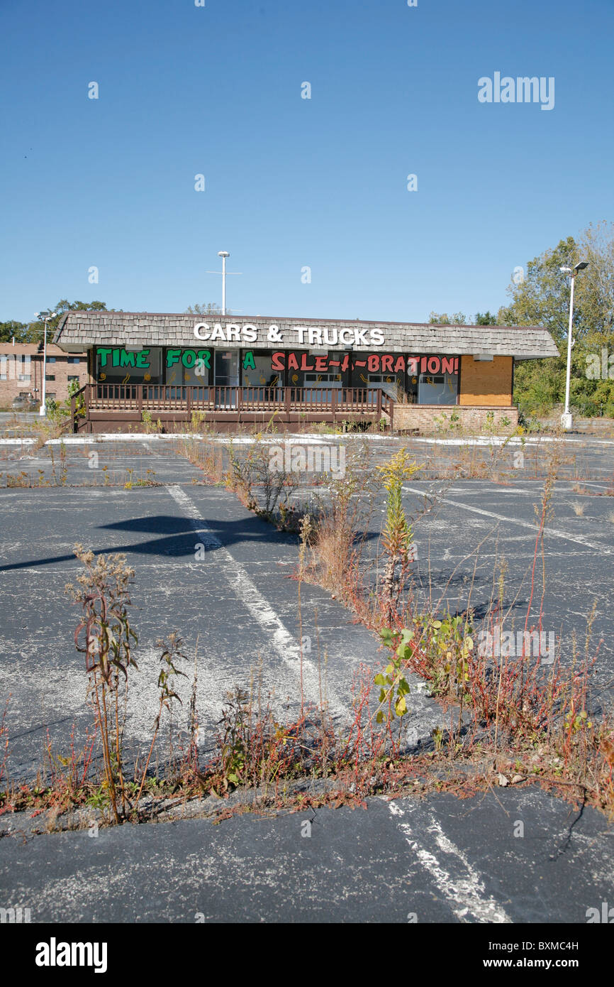 Empty abandoned car and truck dealer lot with weeds growing. Sign reads ...