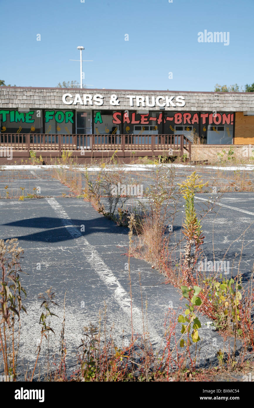 Empty abandoned car and truck dealer lot with weeds growing. Sign reads ...