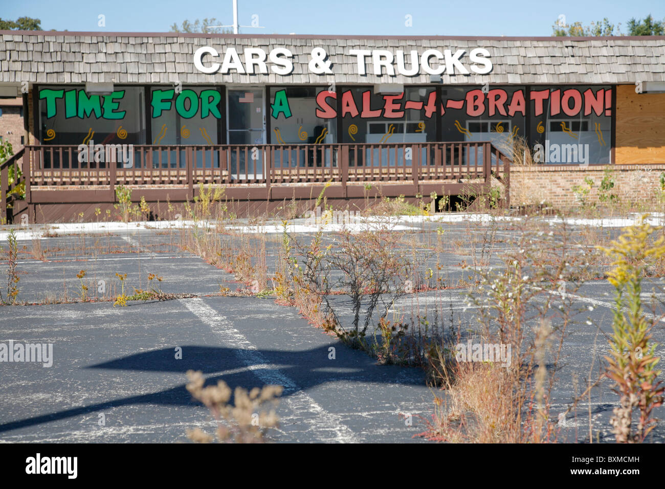Empty abandoned car and truck dealer lot with weeds growing. Sign reads ...