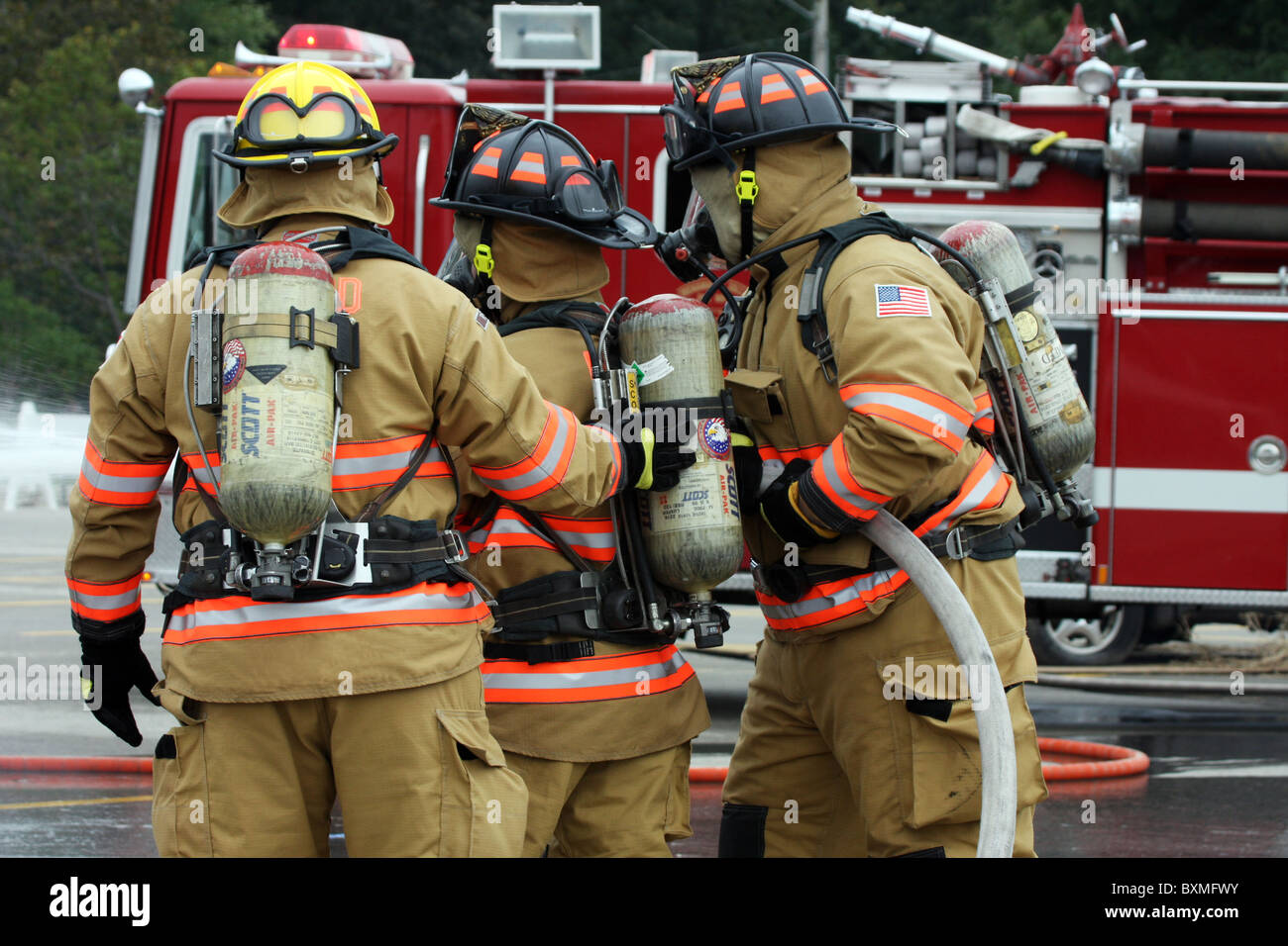 Firefighters on a hose line fighting a fire with water in front of a ...