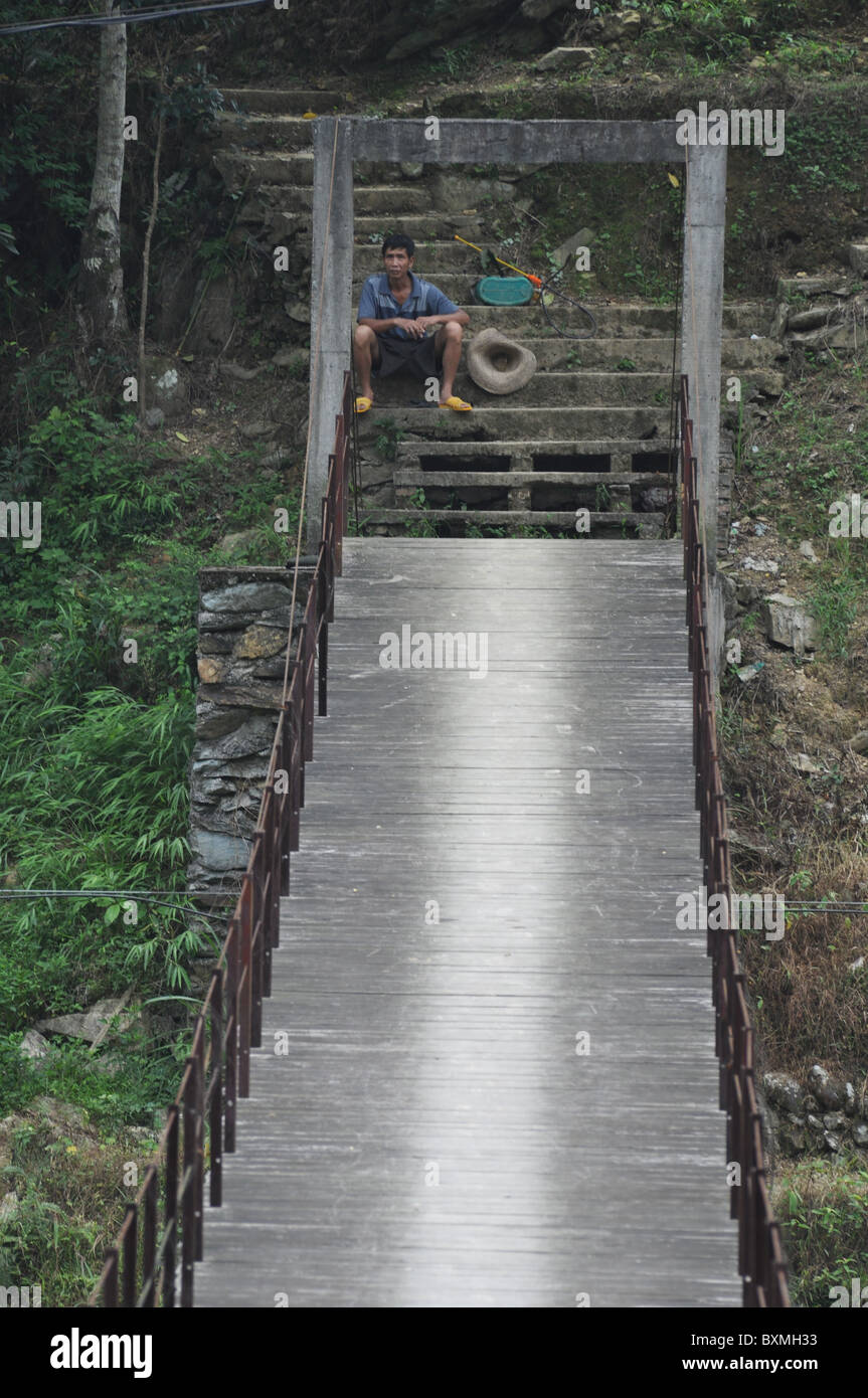 A Chinese man sitting at the end of a very long suspension bridge in ...
