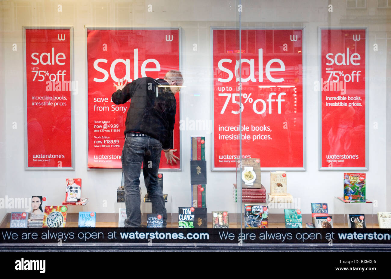 A SHOPKEEPER FROM WHATERSTONE IS HANGING A SALE SIGN IN HIS SHOP WINDOW ...