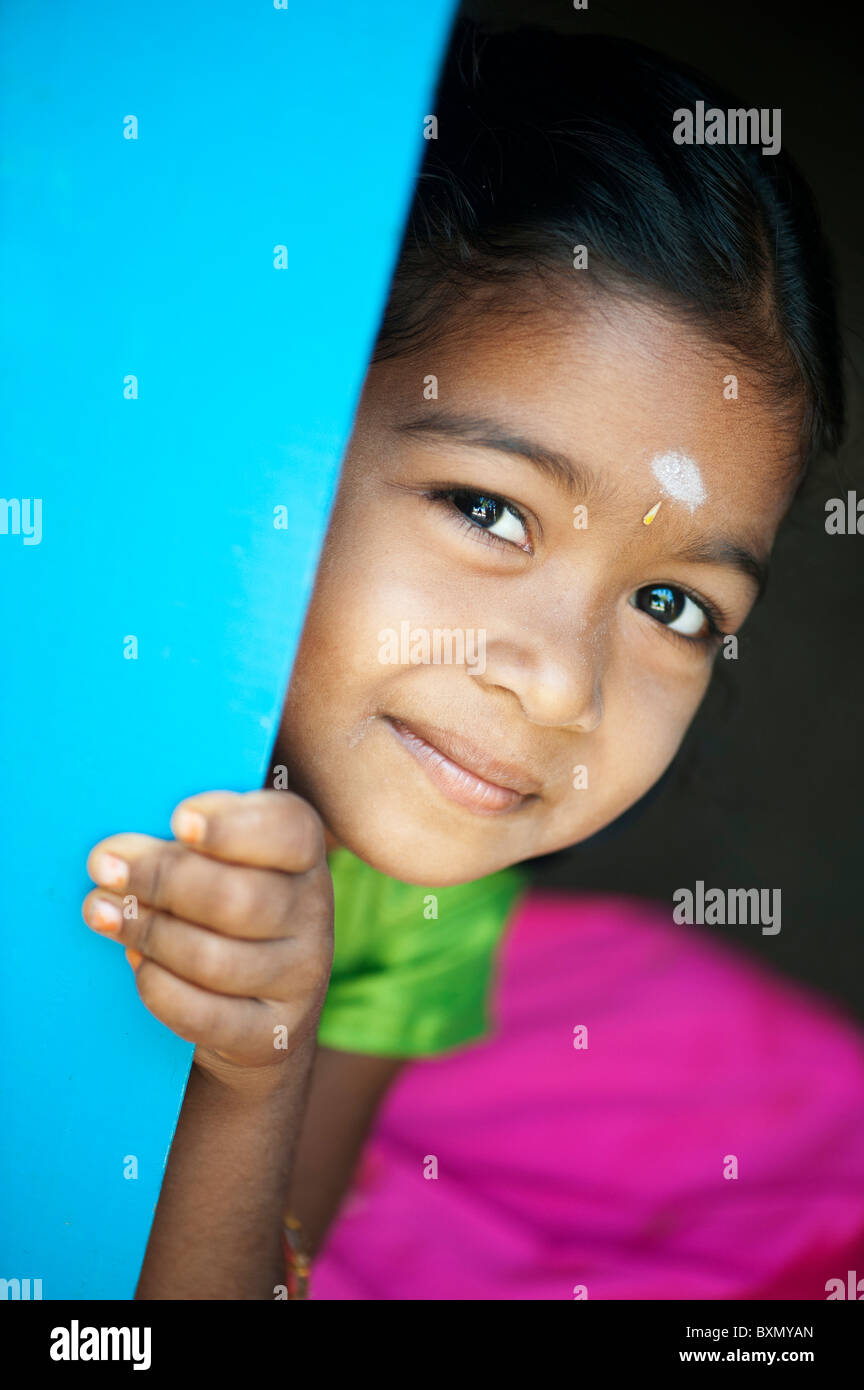 Smiling happy Indian village girl looking round a colourful door ...