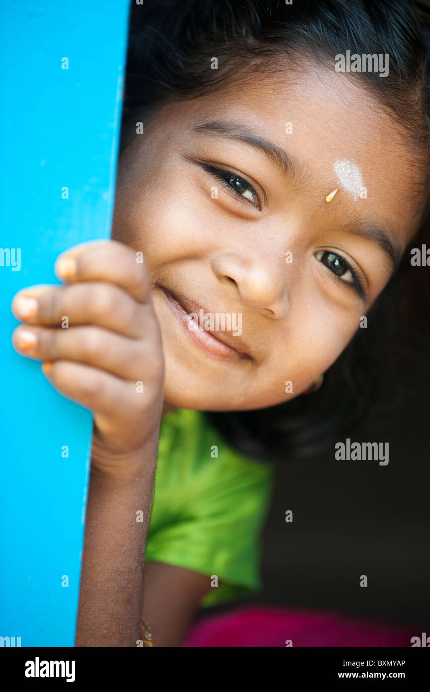 Smiling happy Indian village girl looking round a colourful door ...