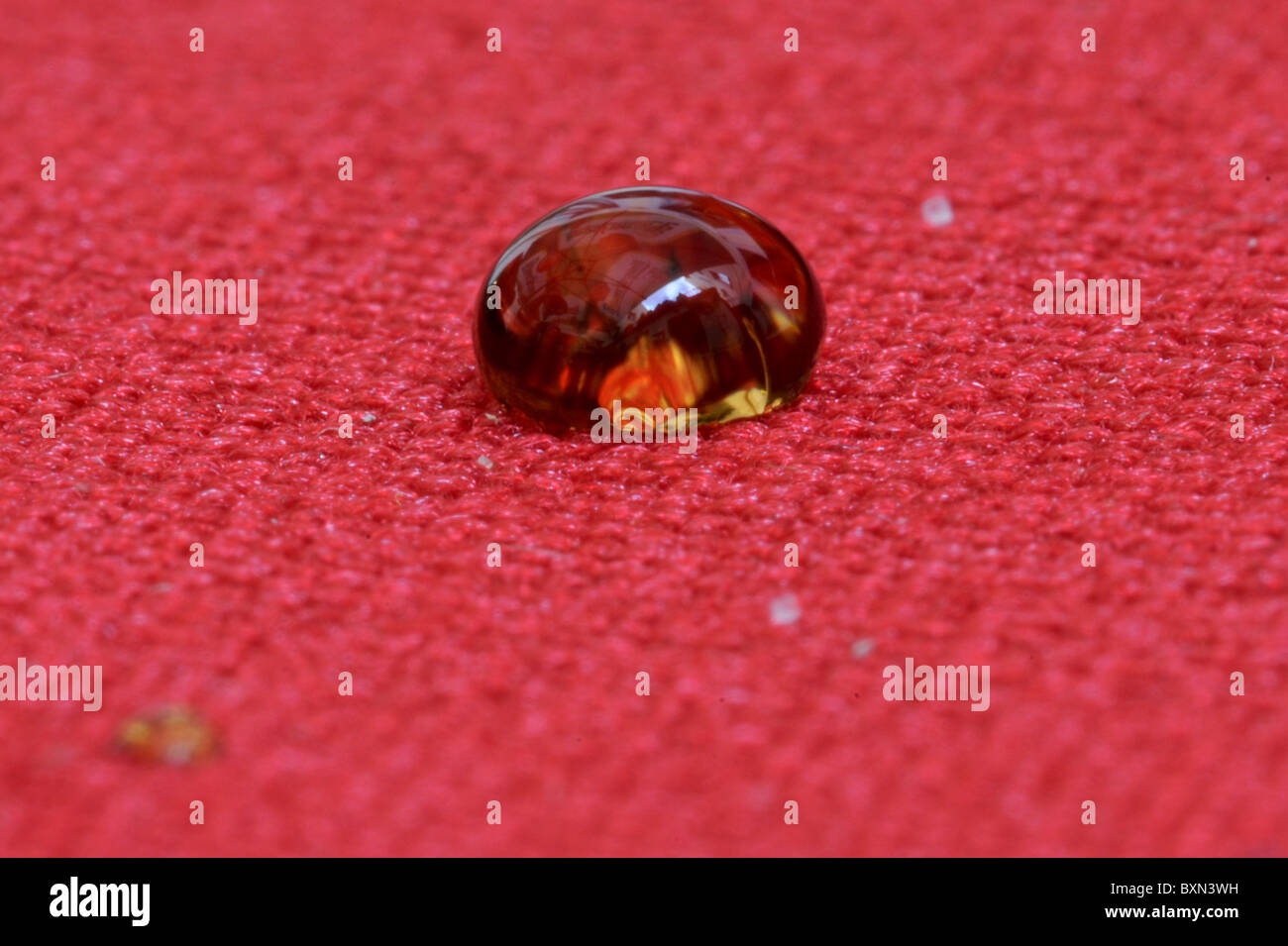 A close-up image of a drop of cola on red fabric showing reflections in ...