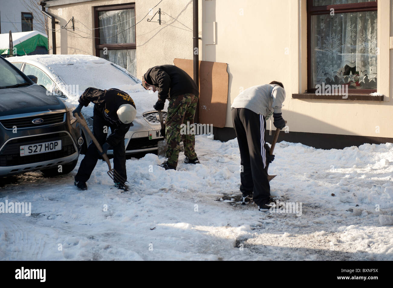 Three people digging with spades clearing snow from their cars ...
