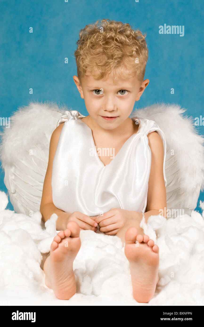 Portrait of cute boy in angel clothes sitting in cloud and looking at ...