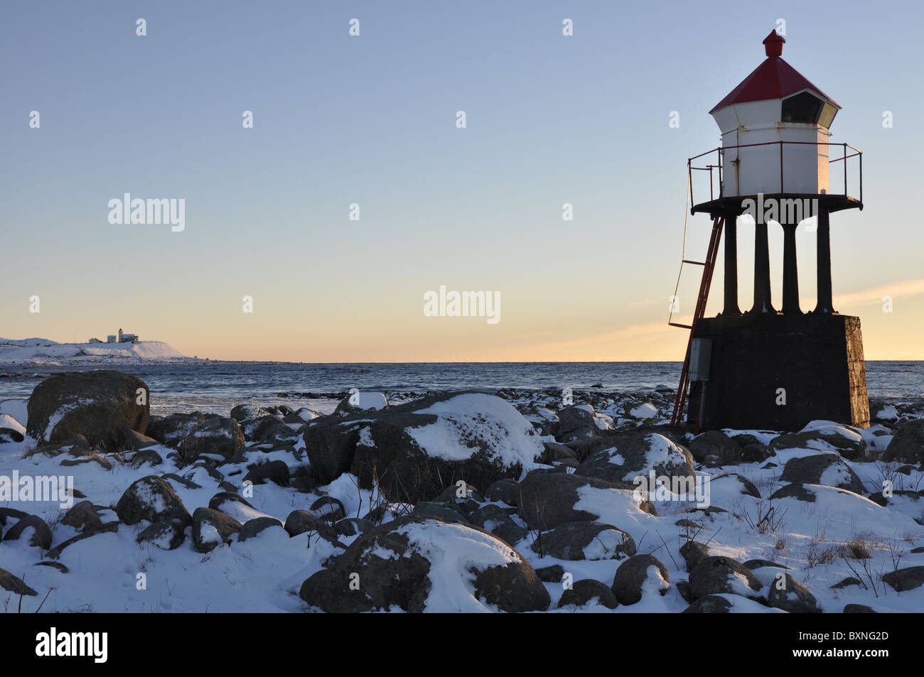 Snow covered landscape by the sea with a lighthouse and rock in sunset ...