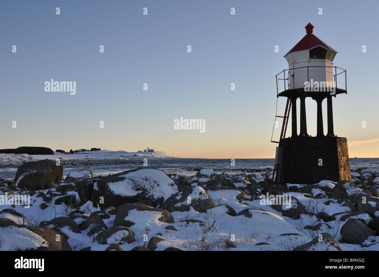 Snow covered landscape by the sea with a lighthouse and rock in sunset ...
