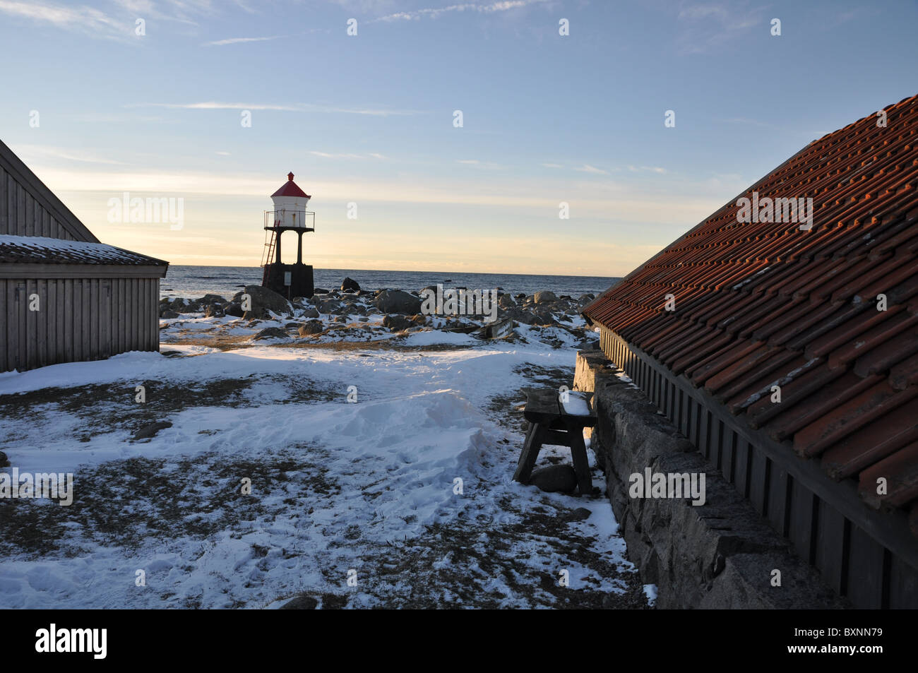 Snow covered landscape by the sea with a lighthouse and rock in sunset ...