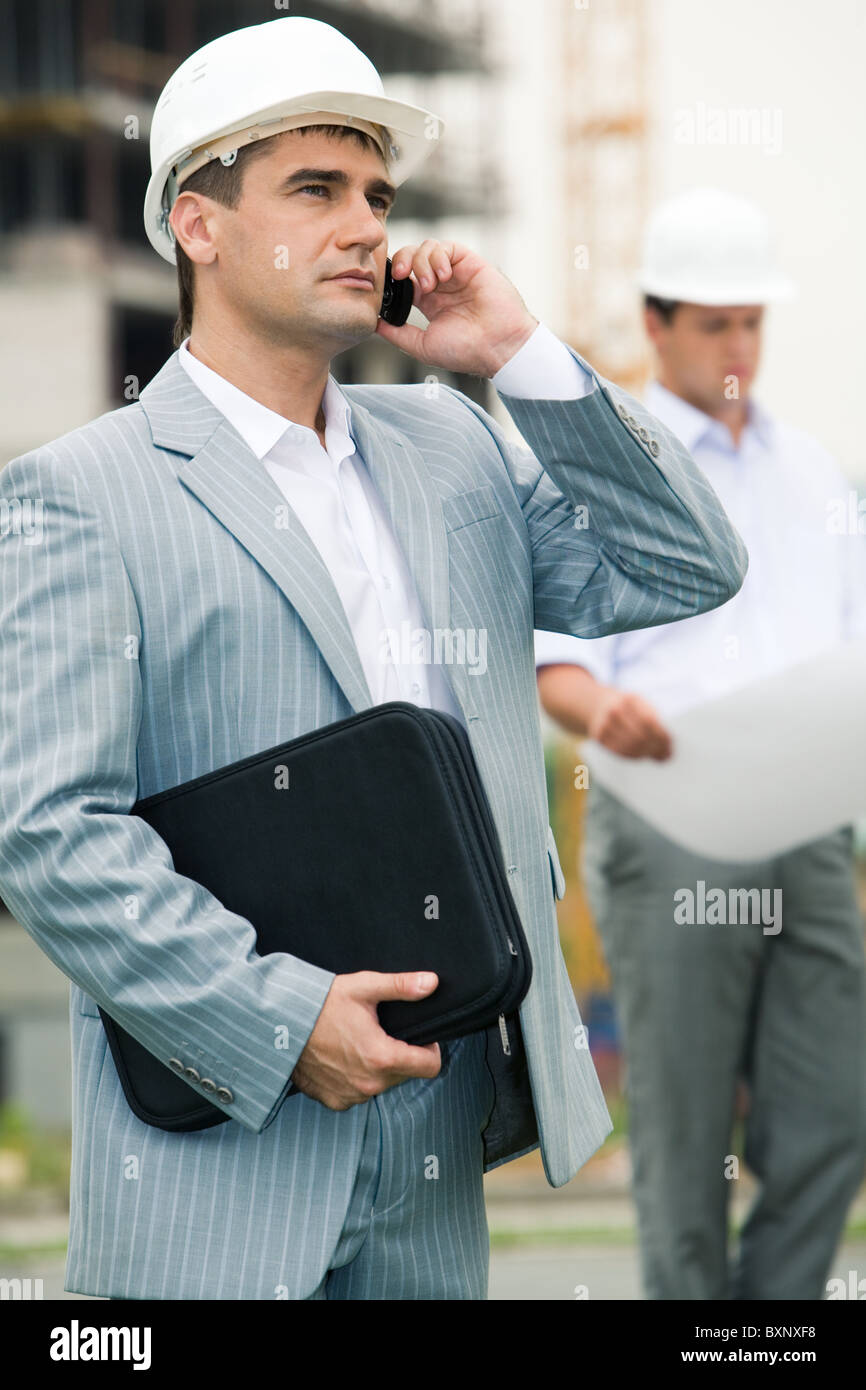 Portrait of busy engineer calling on his mobile phone at building site ...