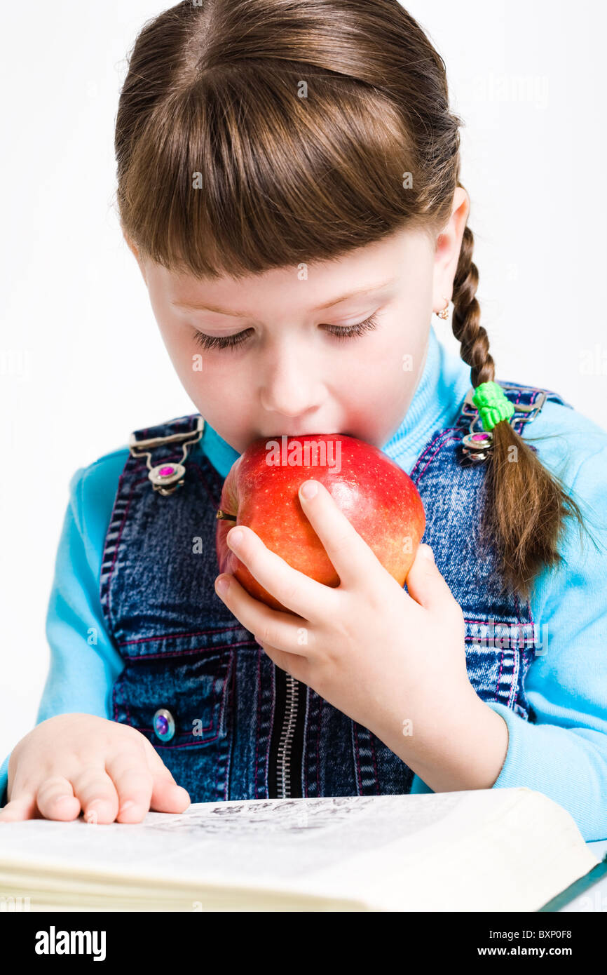Photo of smart schoolgirl reading encyclopedia and eating apple Stock ...