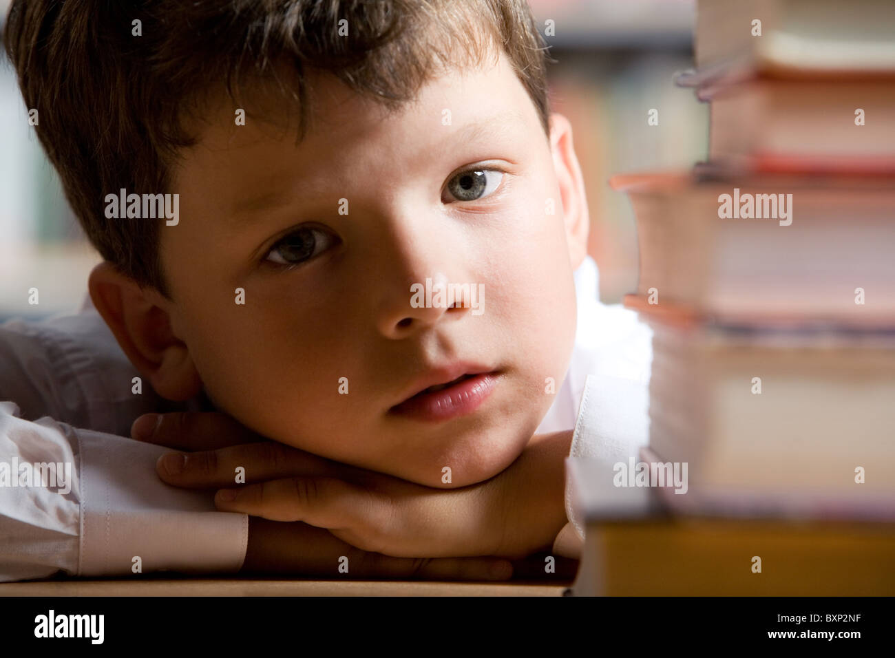 Close-up of little boy’s face with pile of books near by looking at ...