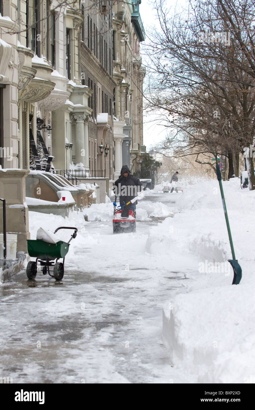 A man using a snow blower to clear the sidewalk in front of a building ...