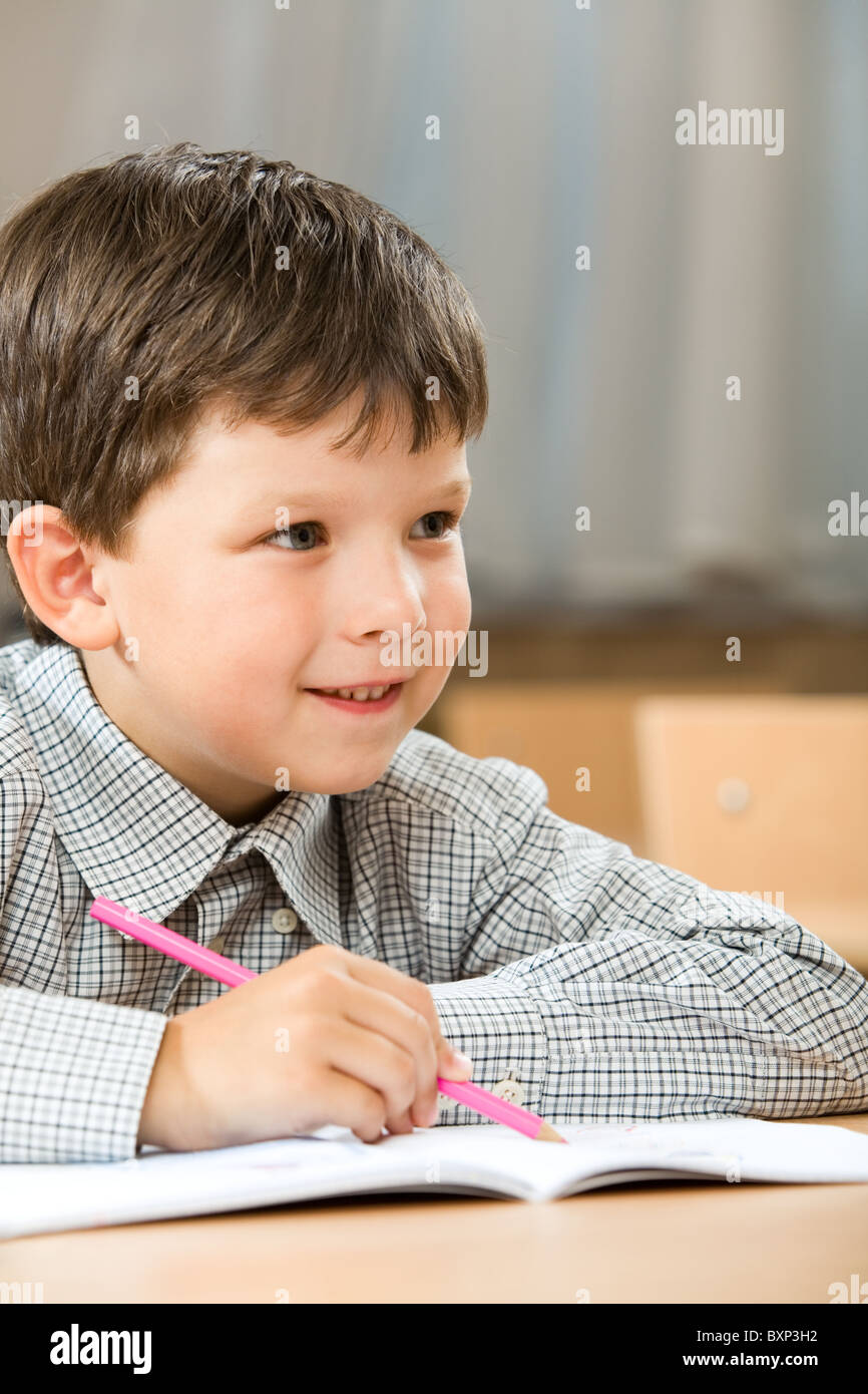 Portrait of smart boy sitting in class and drawing something in ...