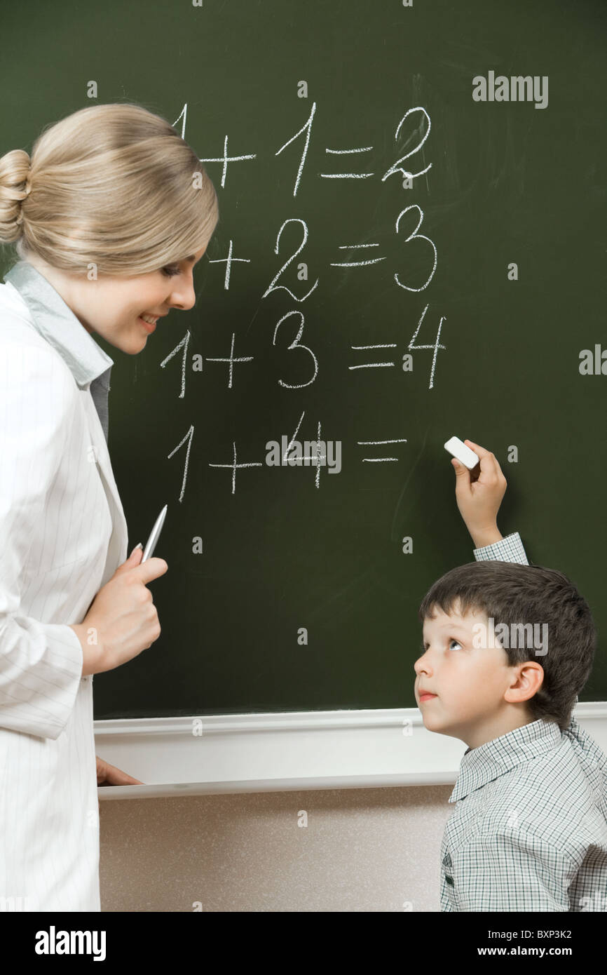 Portrait of diligent pupil looking at his teacher near blackboard while ...