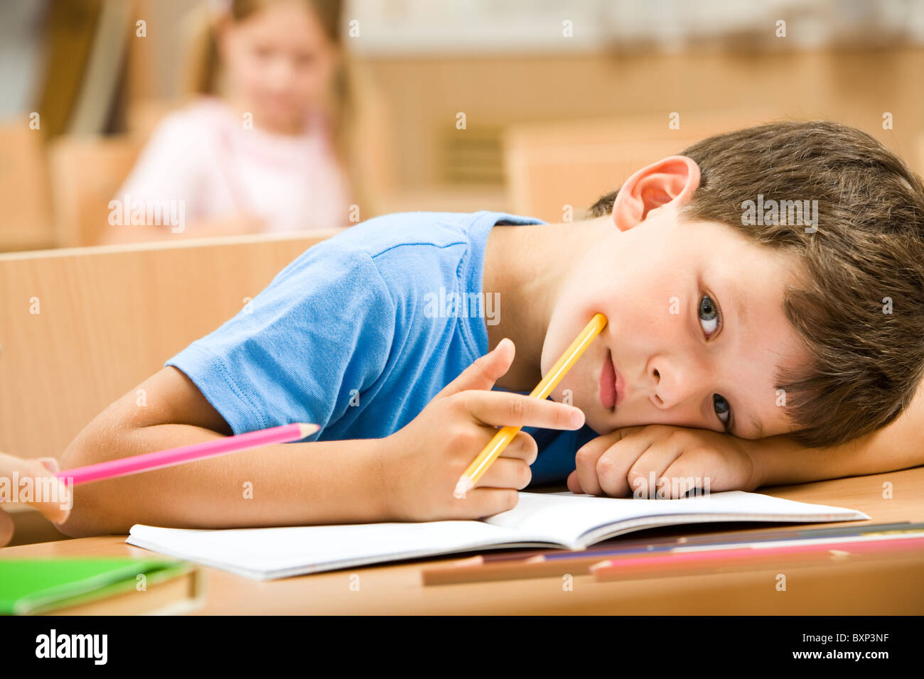 Close-up of tired pupil with yellow crayon putting his head on arm and ...