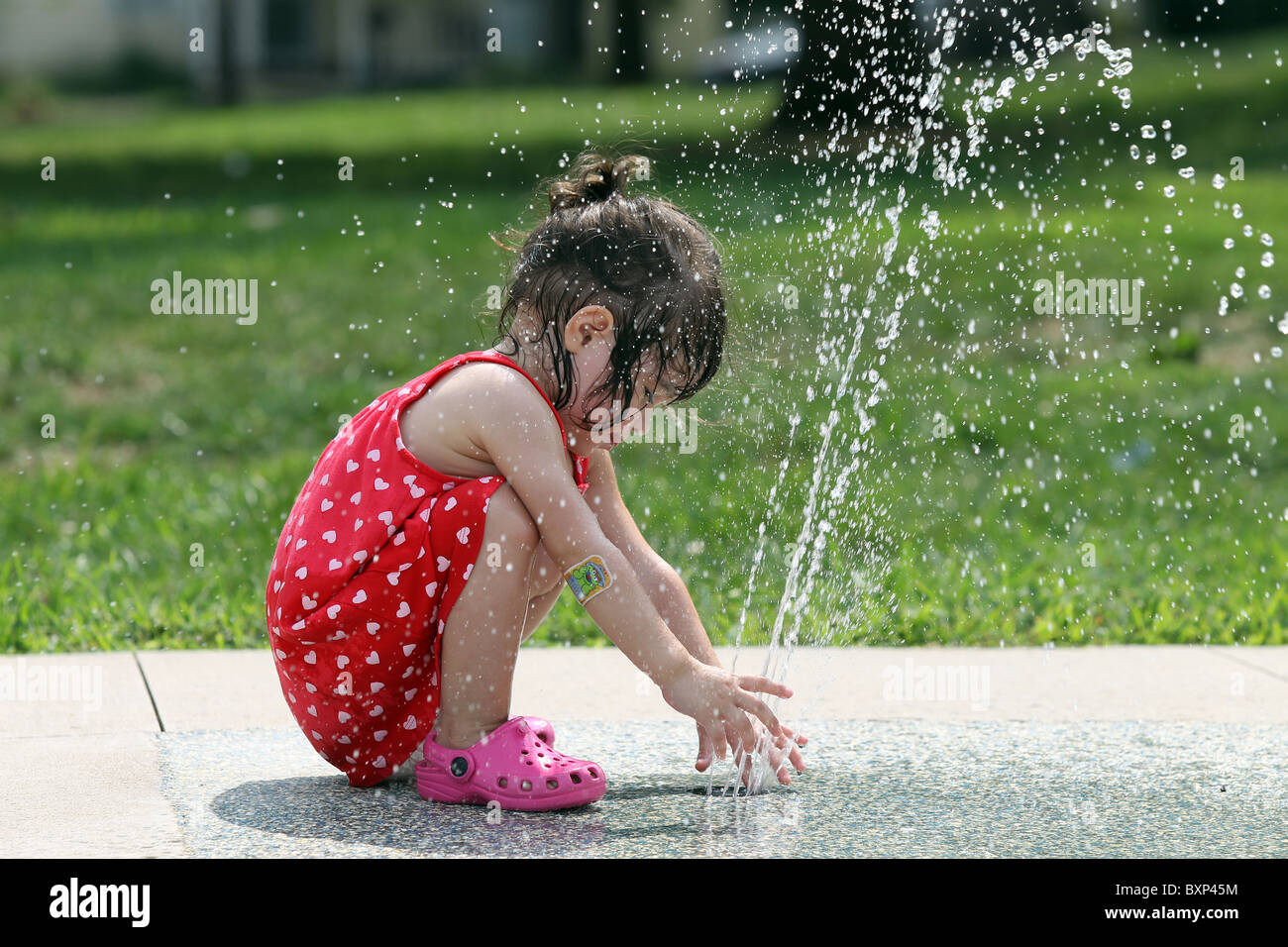 A little girl enjoys her day playing at a local spray park in ...