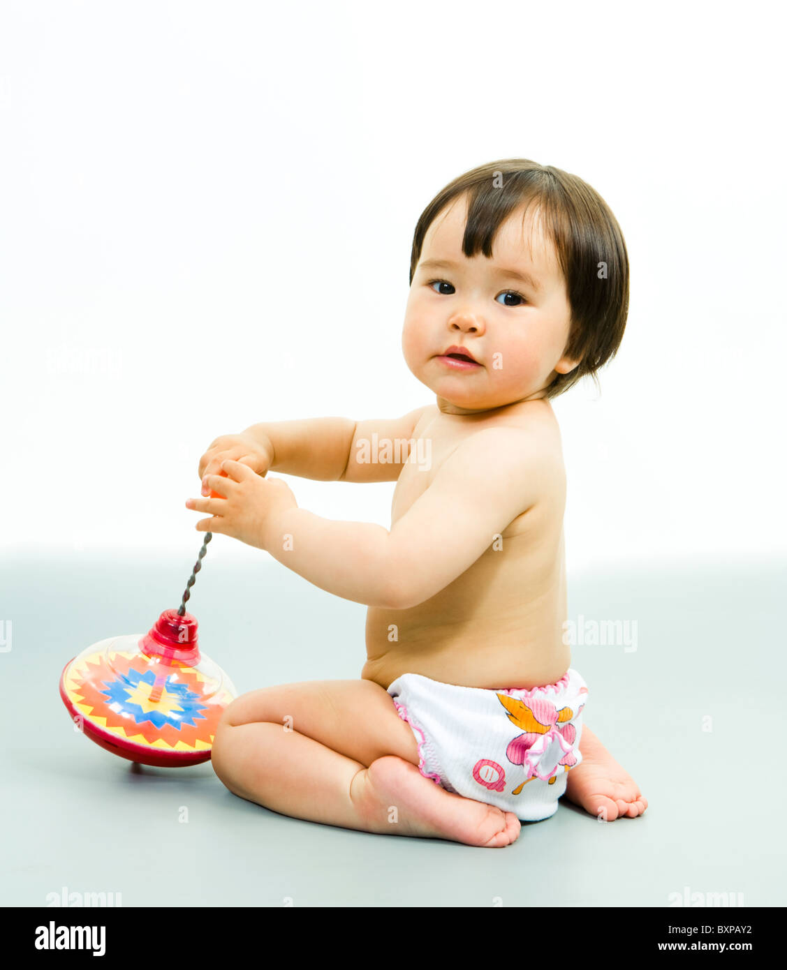Photo of cute baby sitting in the floor and playing with whirling top ...