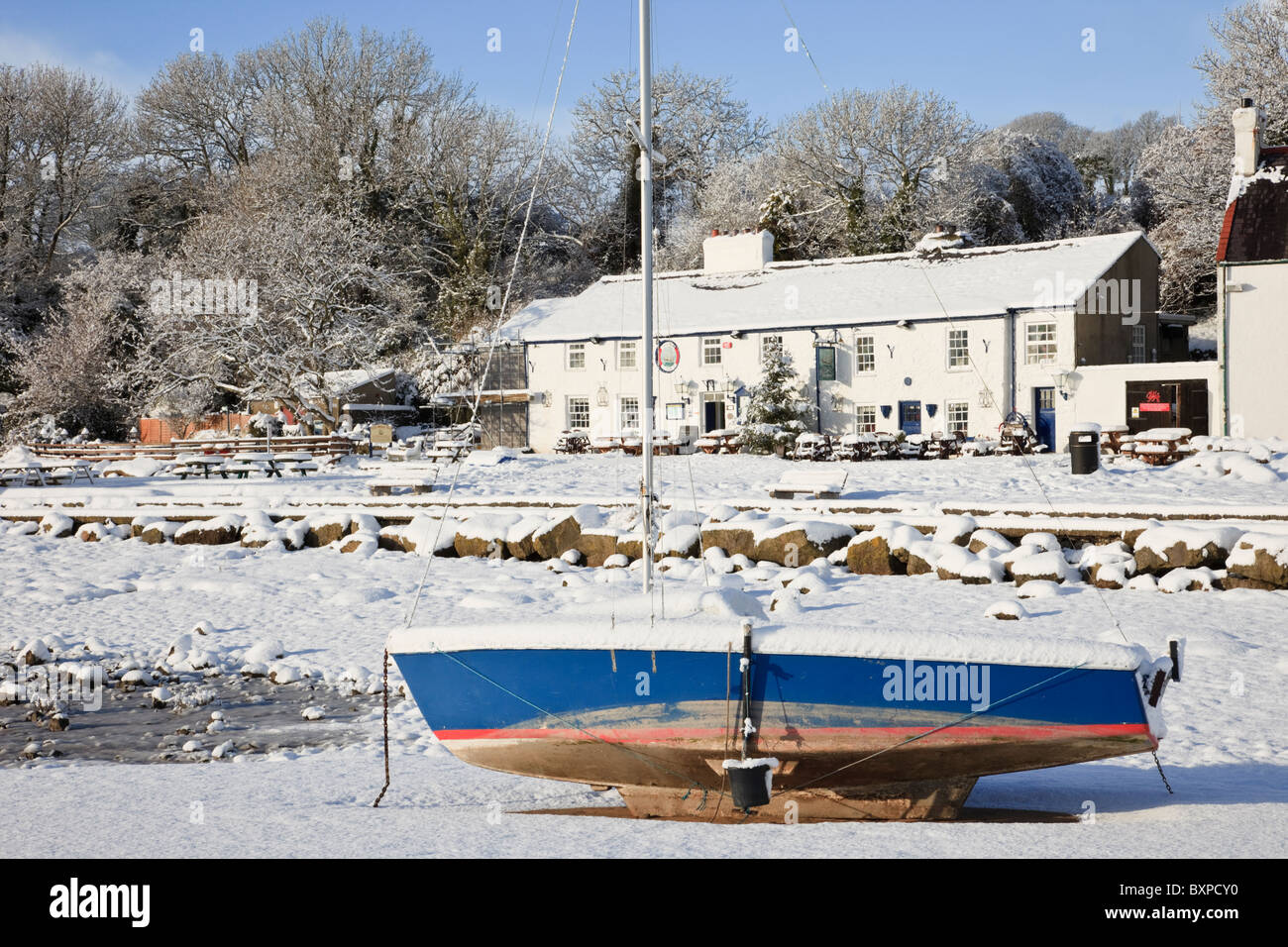 Moored yacht and The Ship Inn with snow in winter in Red Wharf Bay ...